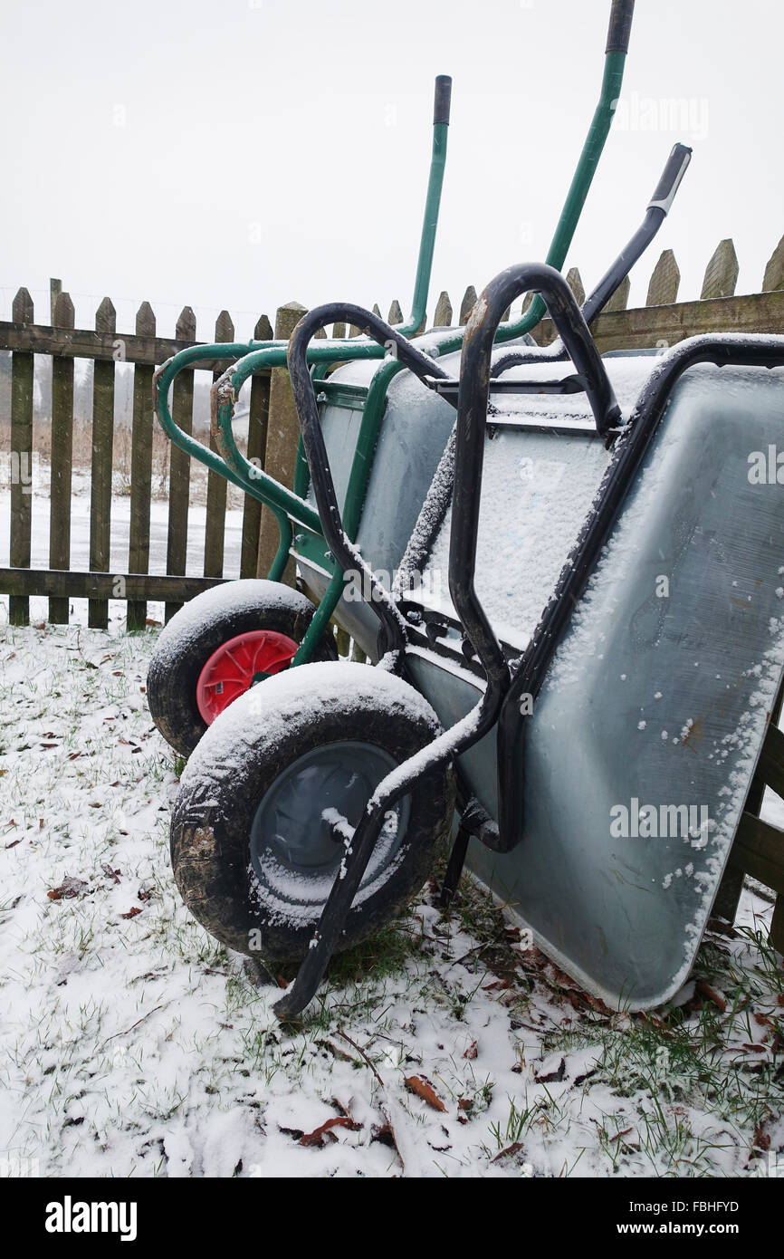 Wheelbarrows in the snow leaning at wooden fence Stock Photo - Alamy