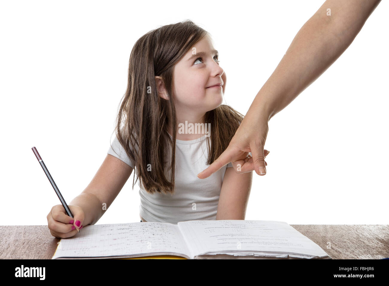 Young girl writing in a book doing her homework with her mum pointing ...