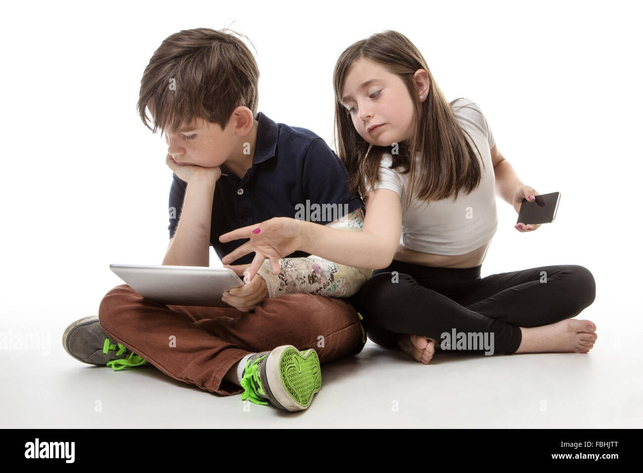 Two children sitting next to each other whilst playing with a mobile ...