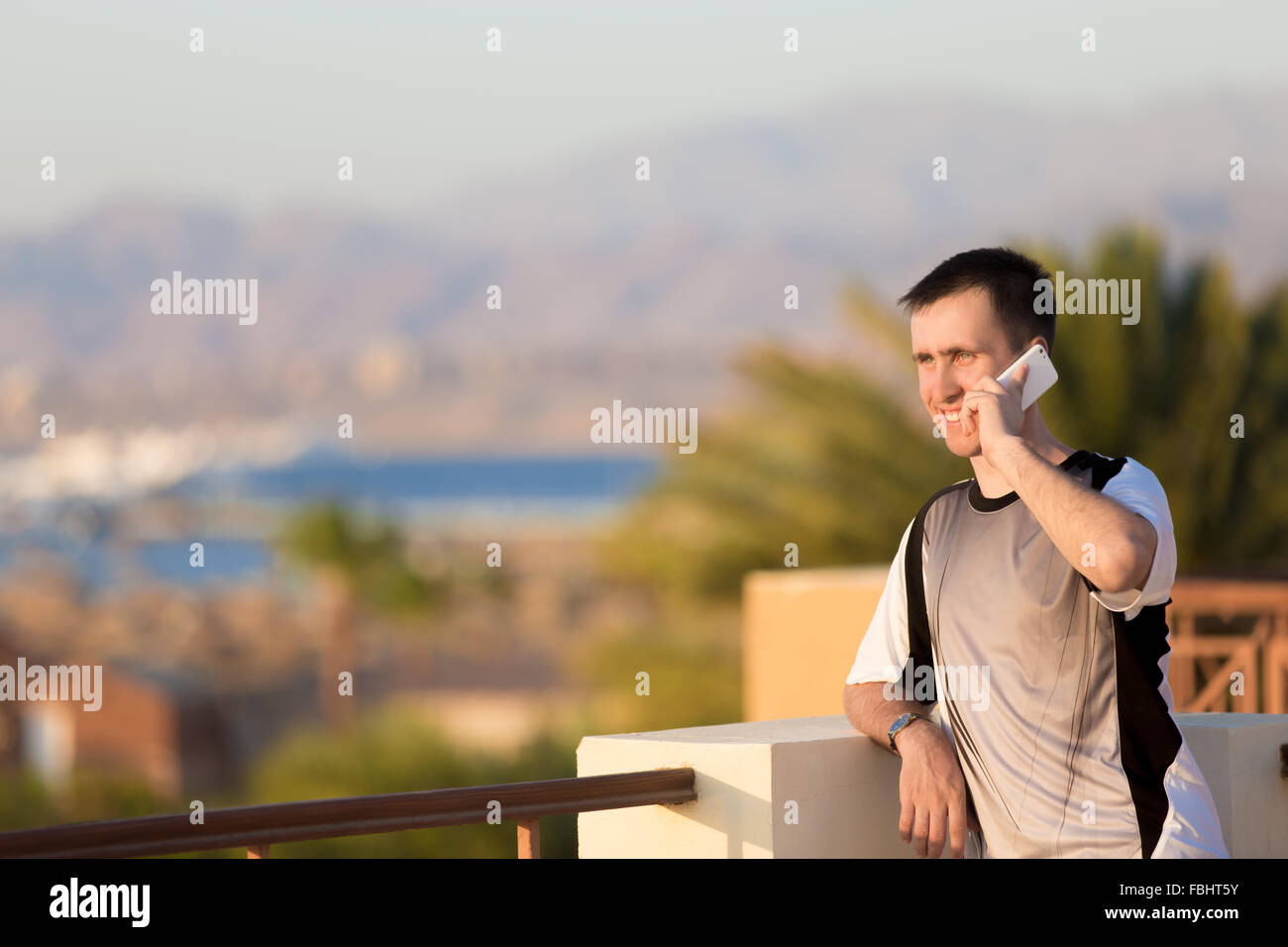 Portrait of young happy smiling man standing in relaxed pose on balcony ...