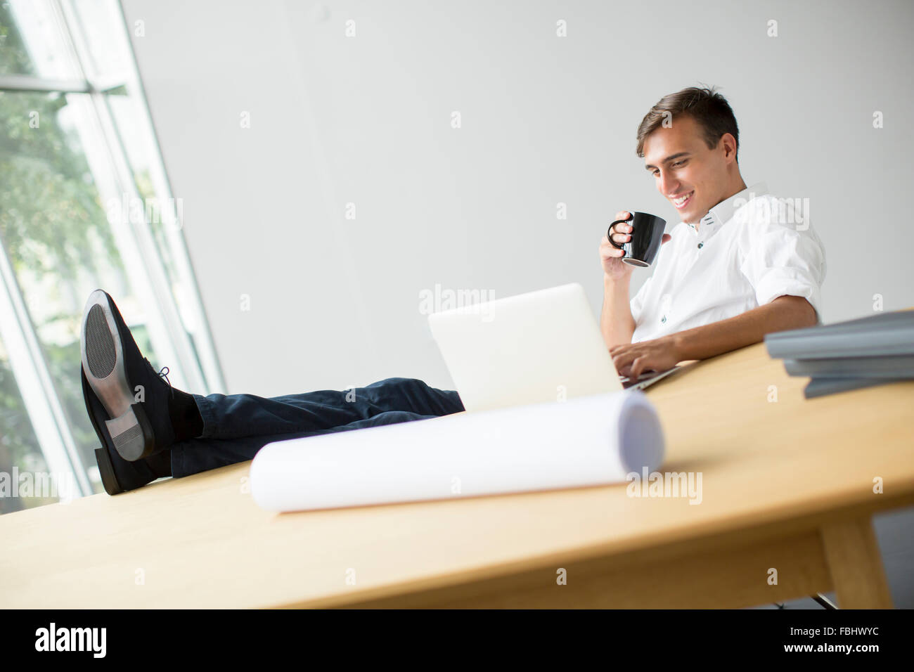 Young man drinking coffee in the office Stock Photo - Alamy