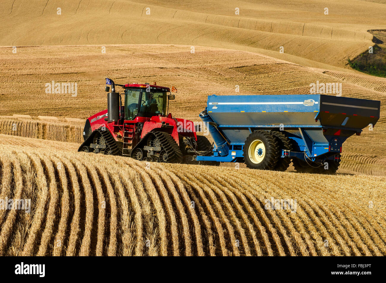 Case track tractor pulling a grain cart during harvest in a grain field ...
