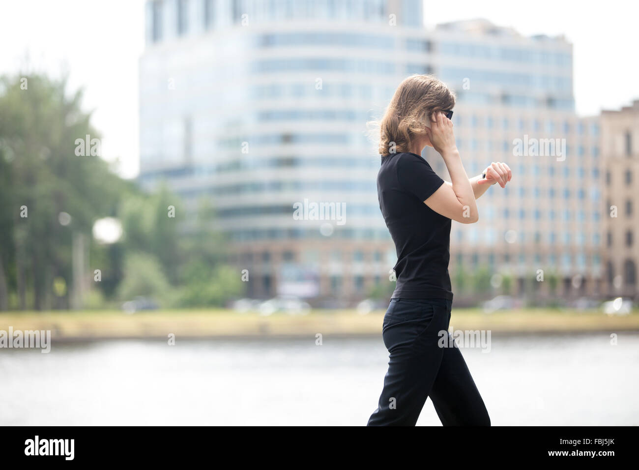 Young confident business woman walking in hurry, looking at watch ...