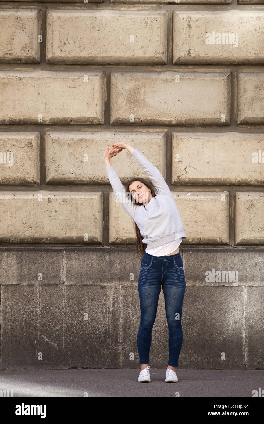 Sporty girl on street working out, doing side bends, standing in ...
