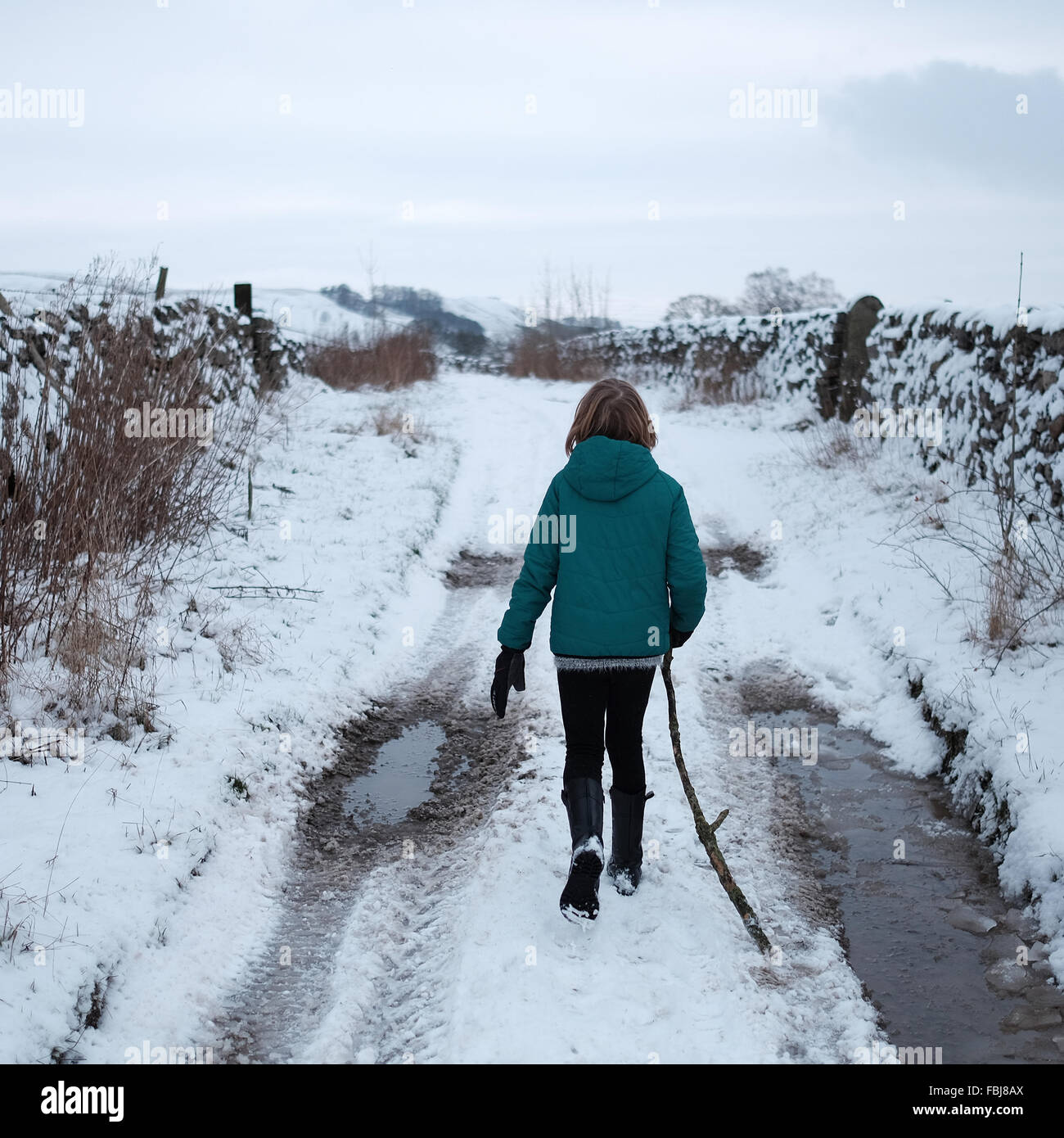 Girl walking along an icy track bordered by walls in the snow and ice ...