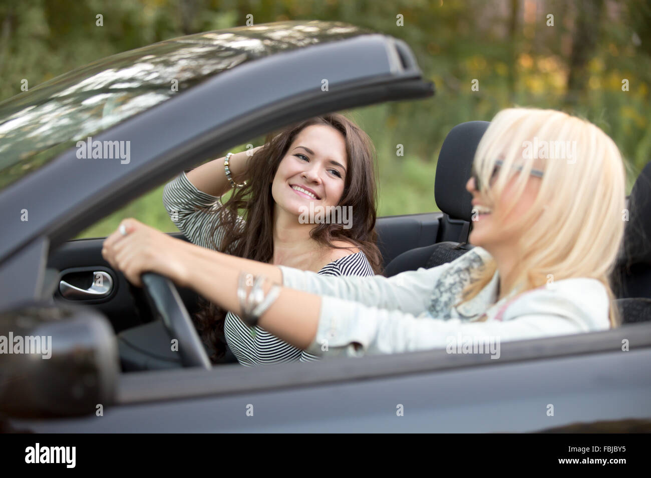 Two beautiful happy traveler young women riding sports car, talking ...