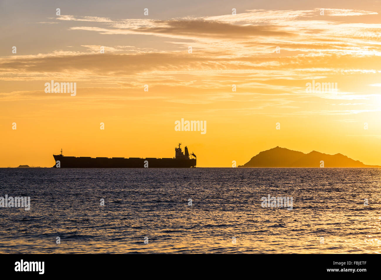 Sun setting at the sea with cargo ship sailing Stock Photo - Alamy