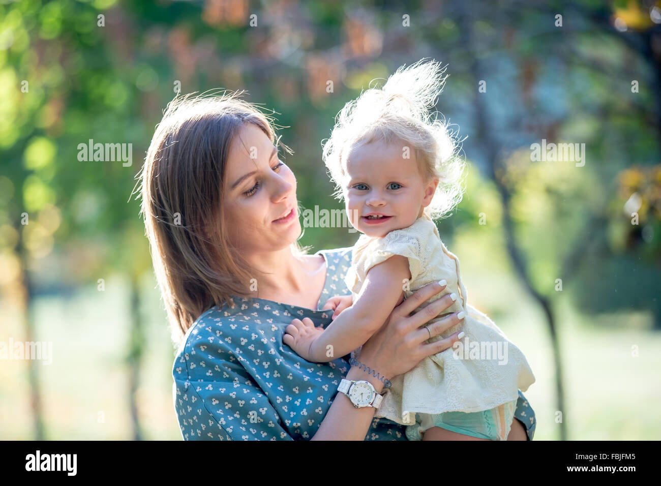 Portrait of young smiling mother holding cute happy toddler daughter wearing dress, hugging ...