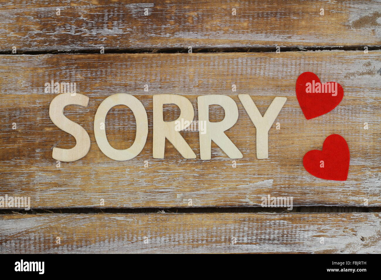 Sorry written with wooden letters and two red hearts on rustic surface ...