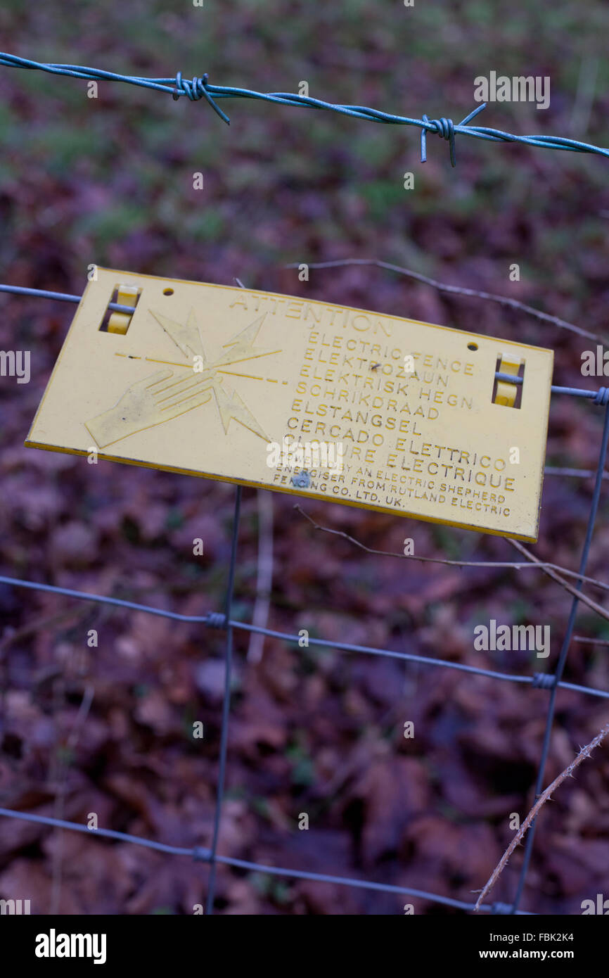 Yellow plastic electric fence warning tag on barbed wire fence in ...