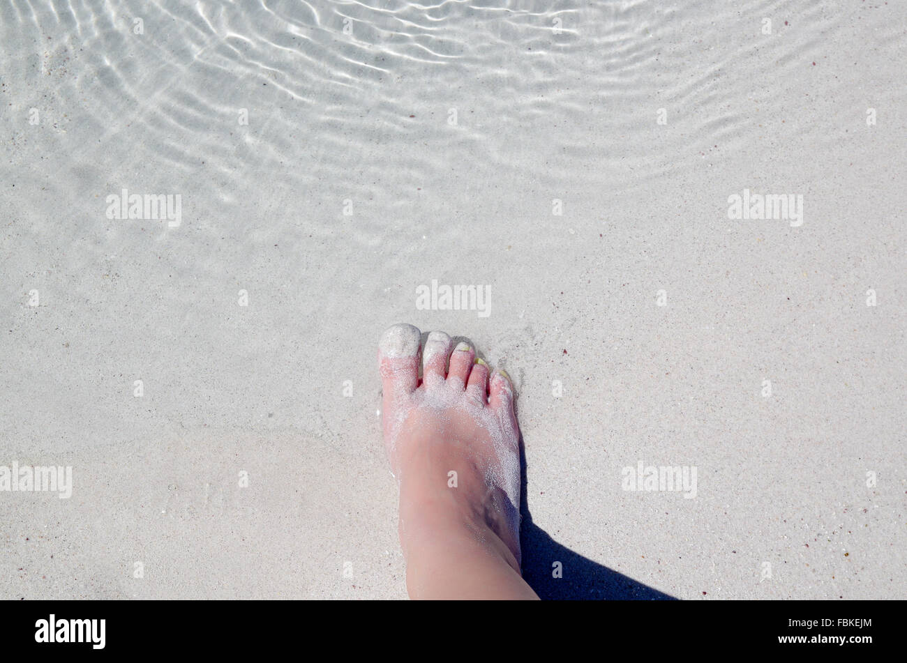 Closeup of right foot stepping into water on beautifully colored sandy ...