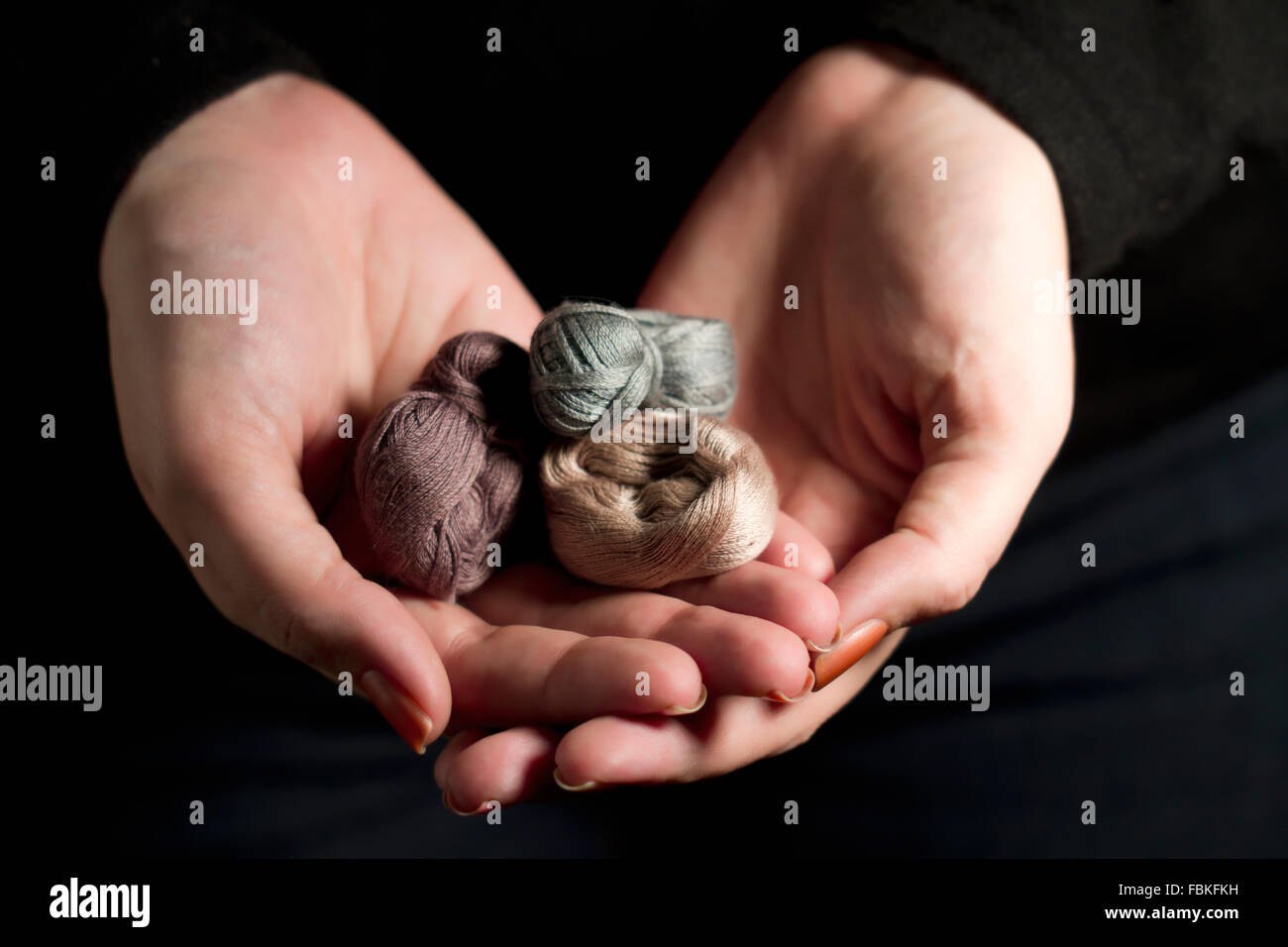 Hands holding yarn on a black background Stock Photo - Alamy