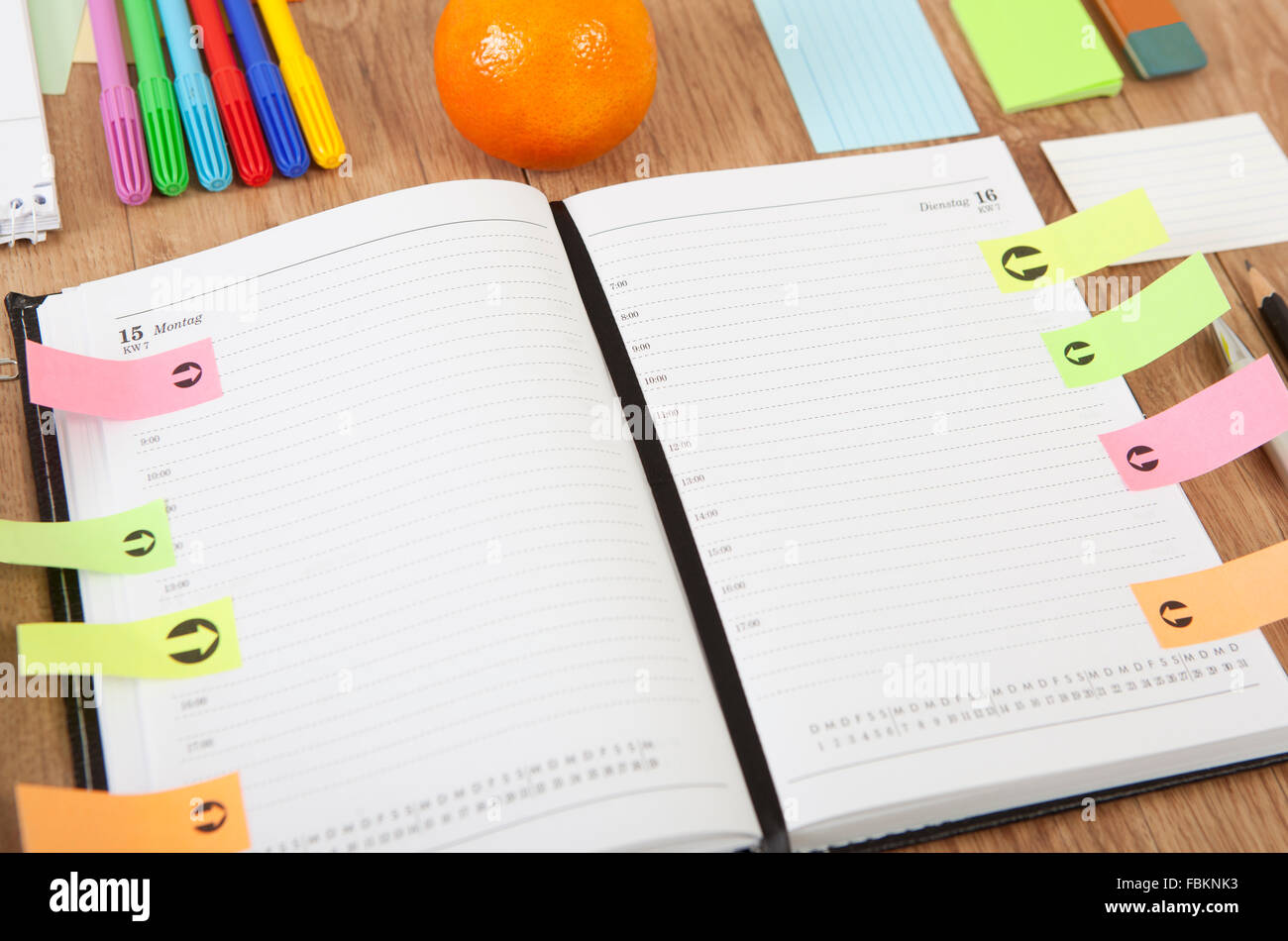 a calendar with Post it is situated on a desk with pencils and fruit ...