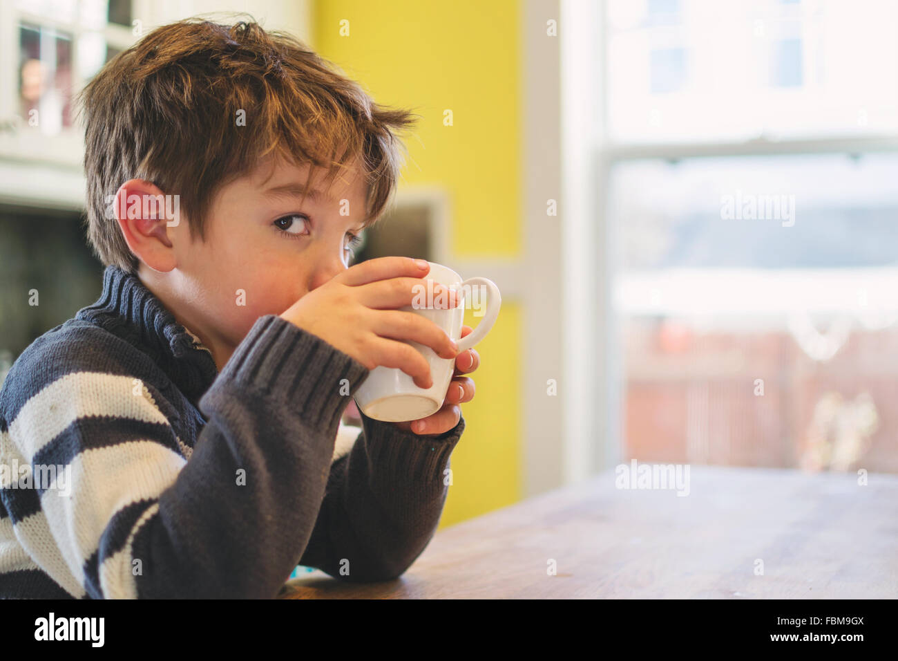 Boy sitting at table drinking a hot drink Stock Photo - Alamy