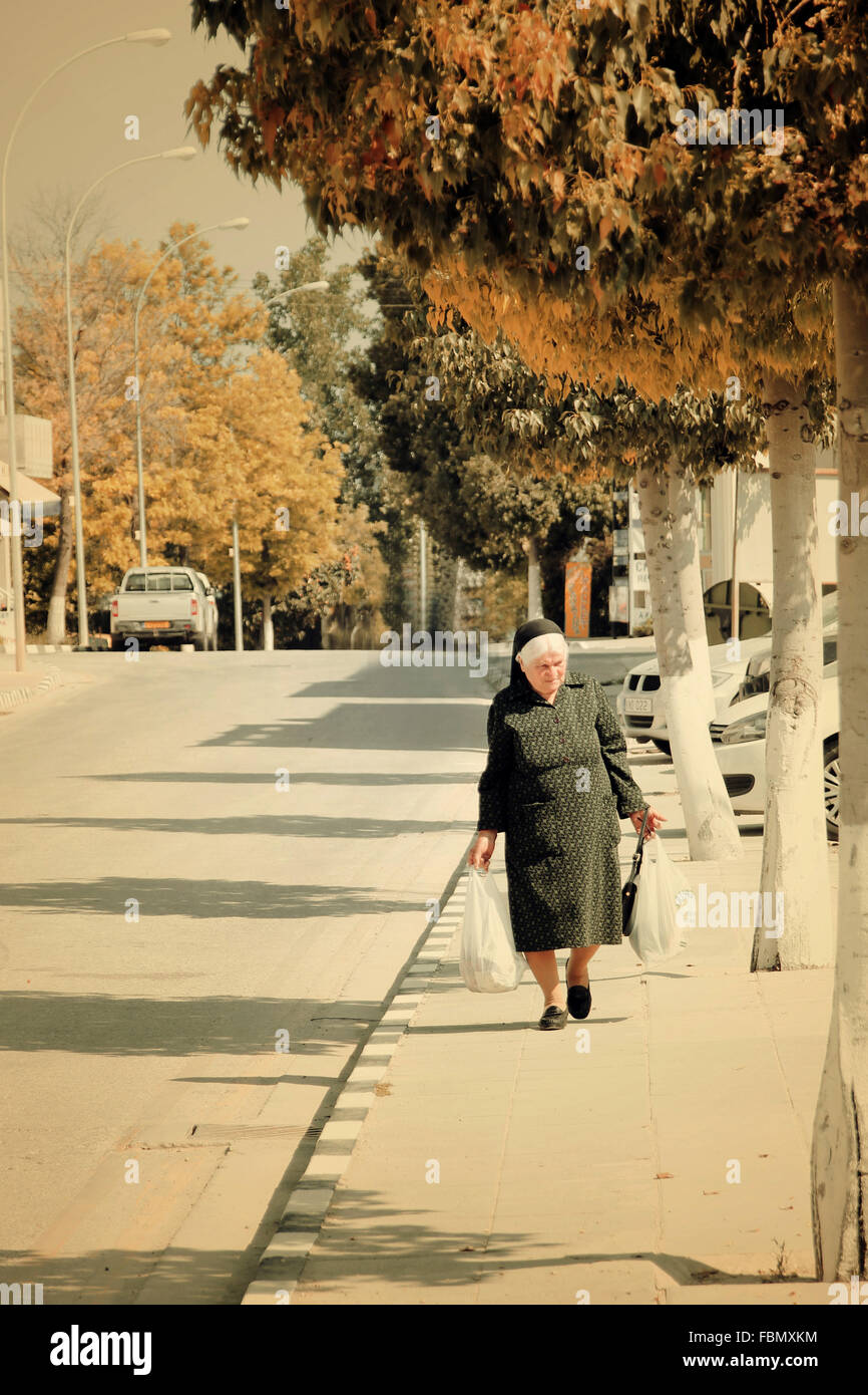 Old lady in black in Cyprus walking along road with shopping bags in ...