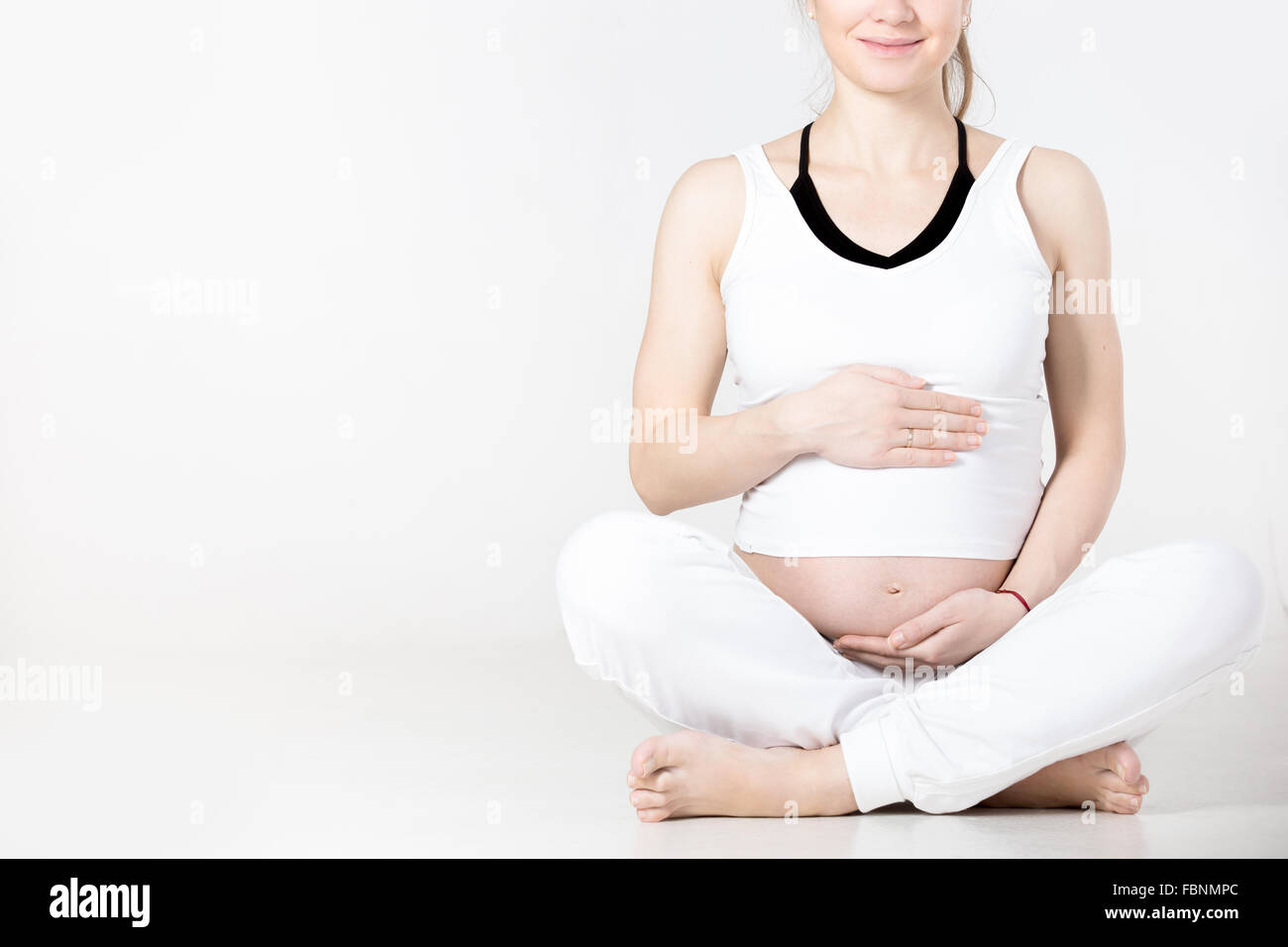 Smiling young pregnant fitness model in sportswear doing yoga or ...