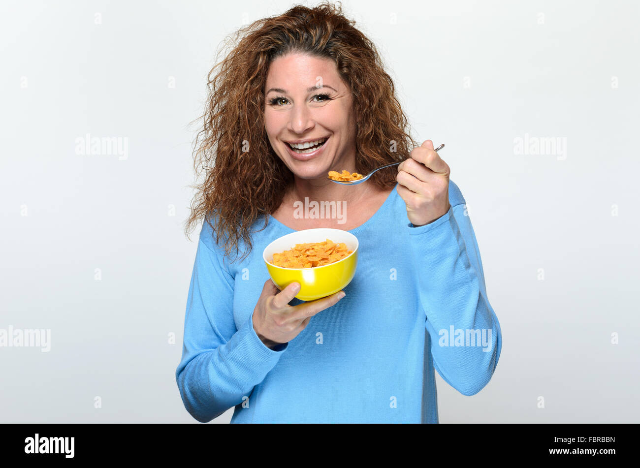 Vivacious young woman eating a handheld bowl breakfast cereal with ...