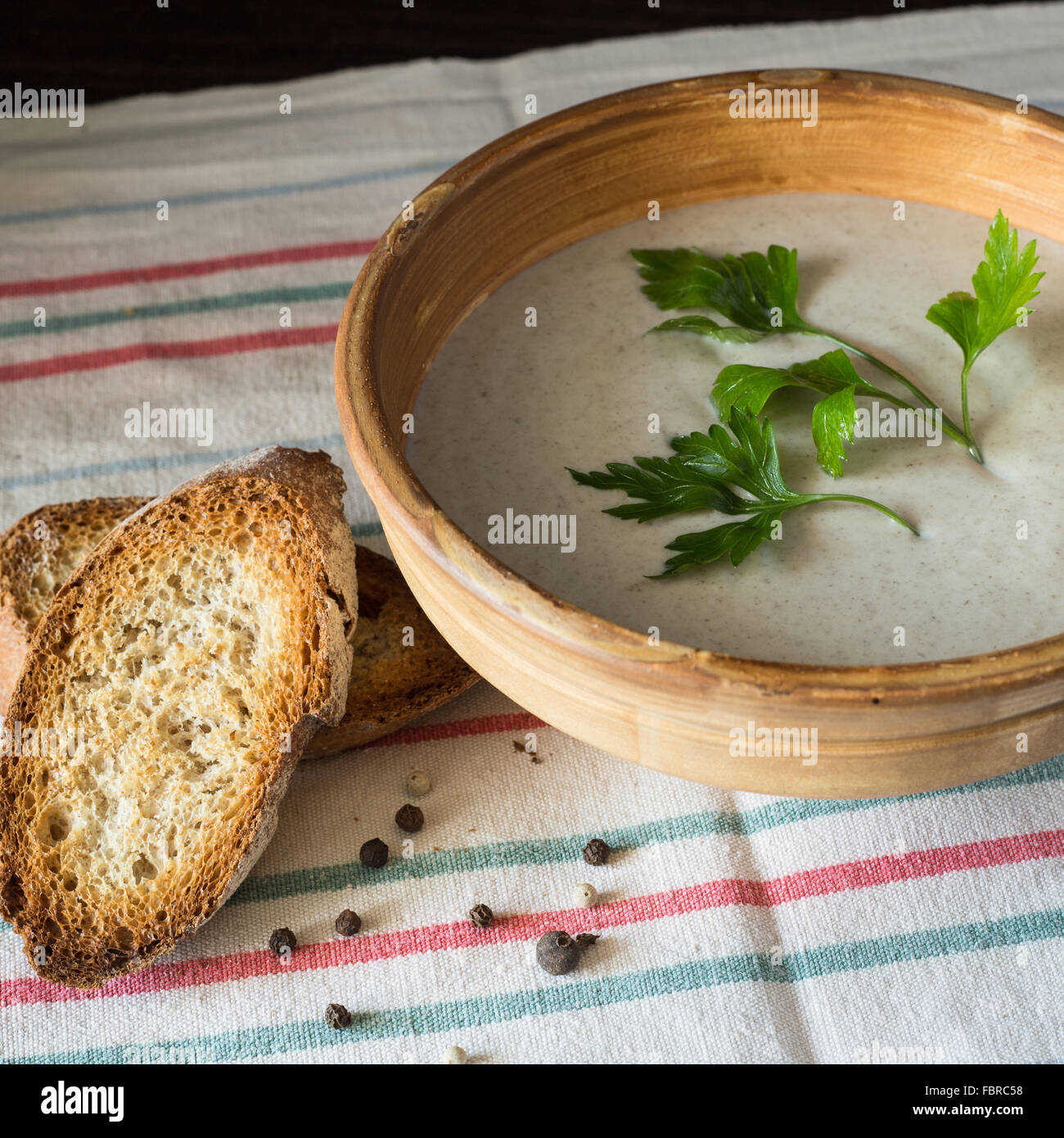 Ceramic bowl with mushroom soup puree with sliced bread on rural ...