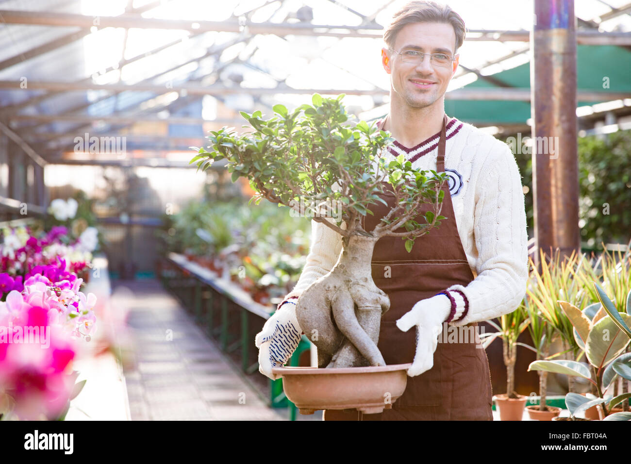 Portrait of attractive happy male gardener in apron and gloves standing ...