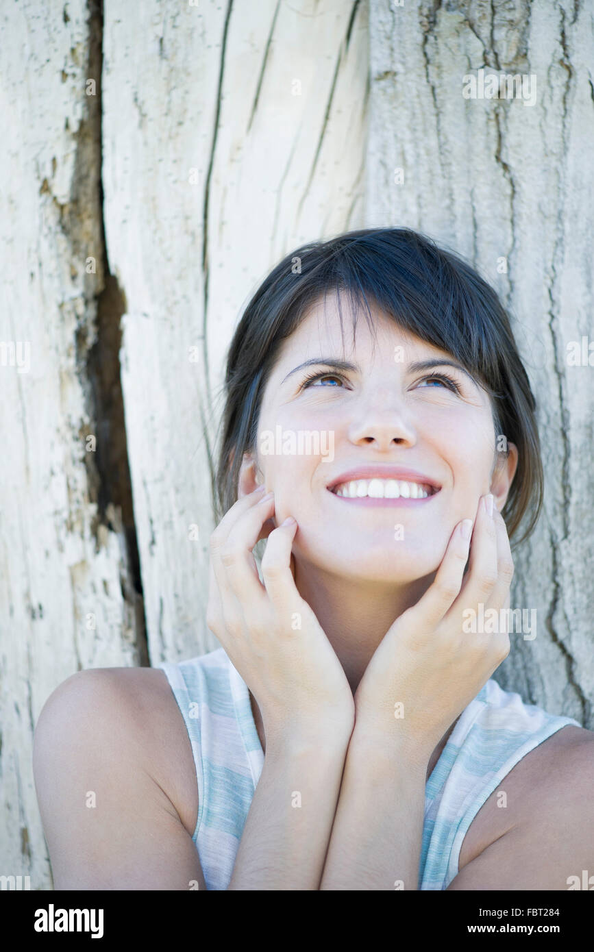 Woman Leaning Against Tree Trunk Looking Up And Smiling Hopefully