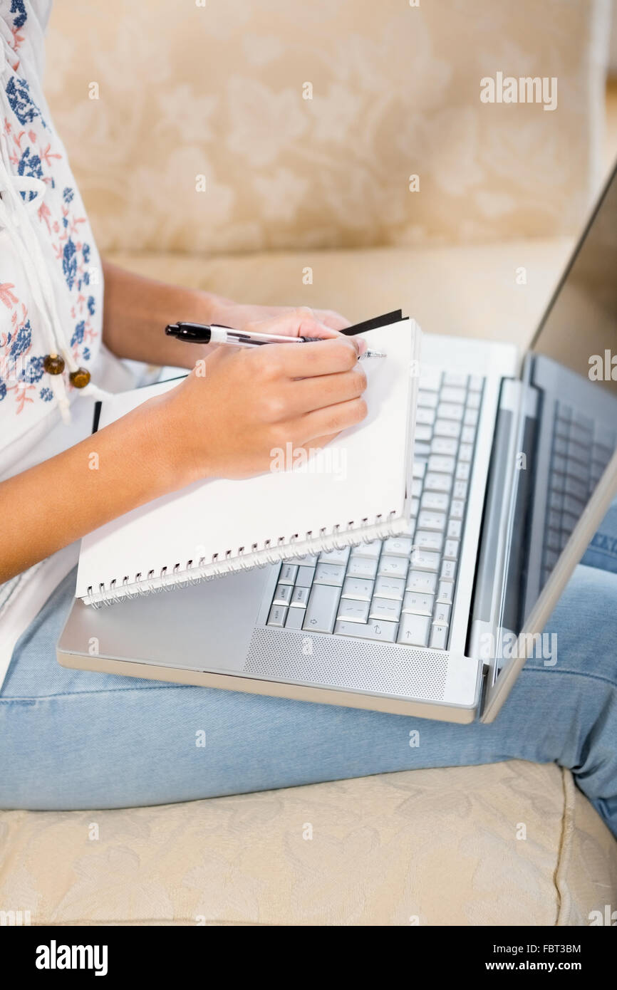 Close up of woman writing on notepad with laptop on her legs Stock ...