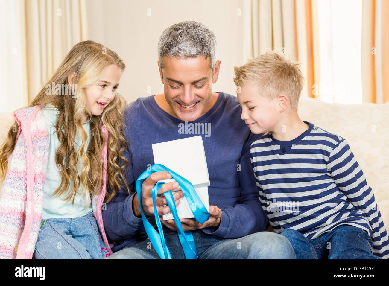 Father opening gift given by children on sofa Stock Photo - Alamy