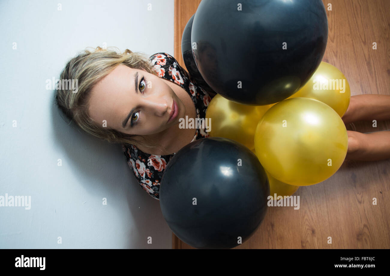 Beautiful model sitting on wooden floor leaning back against white wall ...