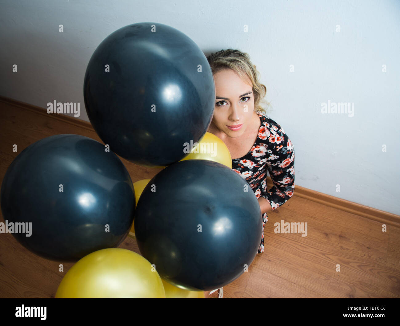 Beautiful model sitting on wooden floor leaning back against white wall ...