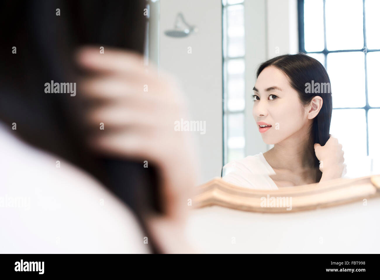 Woman looking in mirror, fixing her hair Stock Photo - Alamy