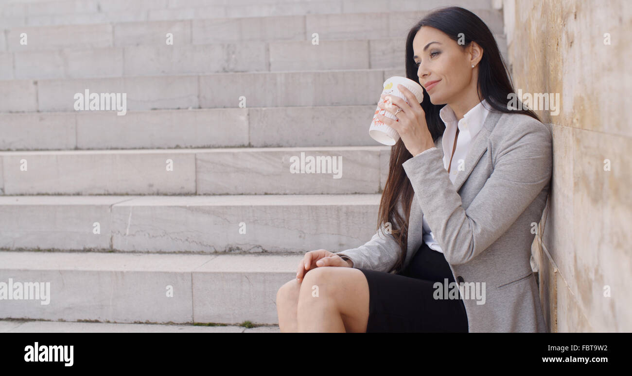 Grinning brunette professional woman sitting on outdoor stairs while ...