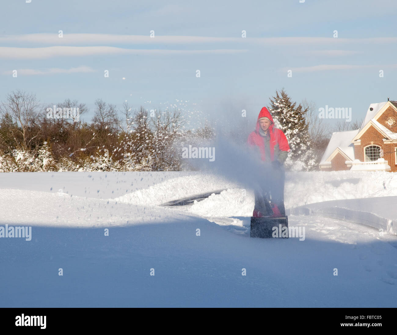 Senior man in red coat using a snow blower during a blizzard on home ...
