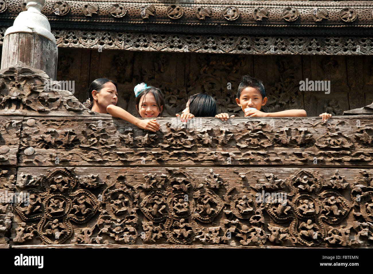 Burmese children peer over the wooden walls in front of the teak carved ...