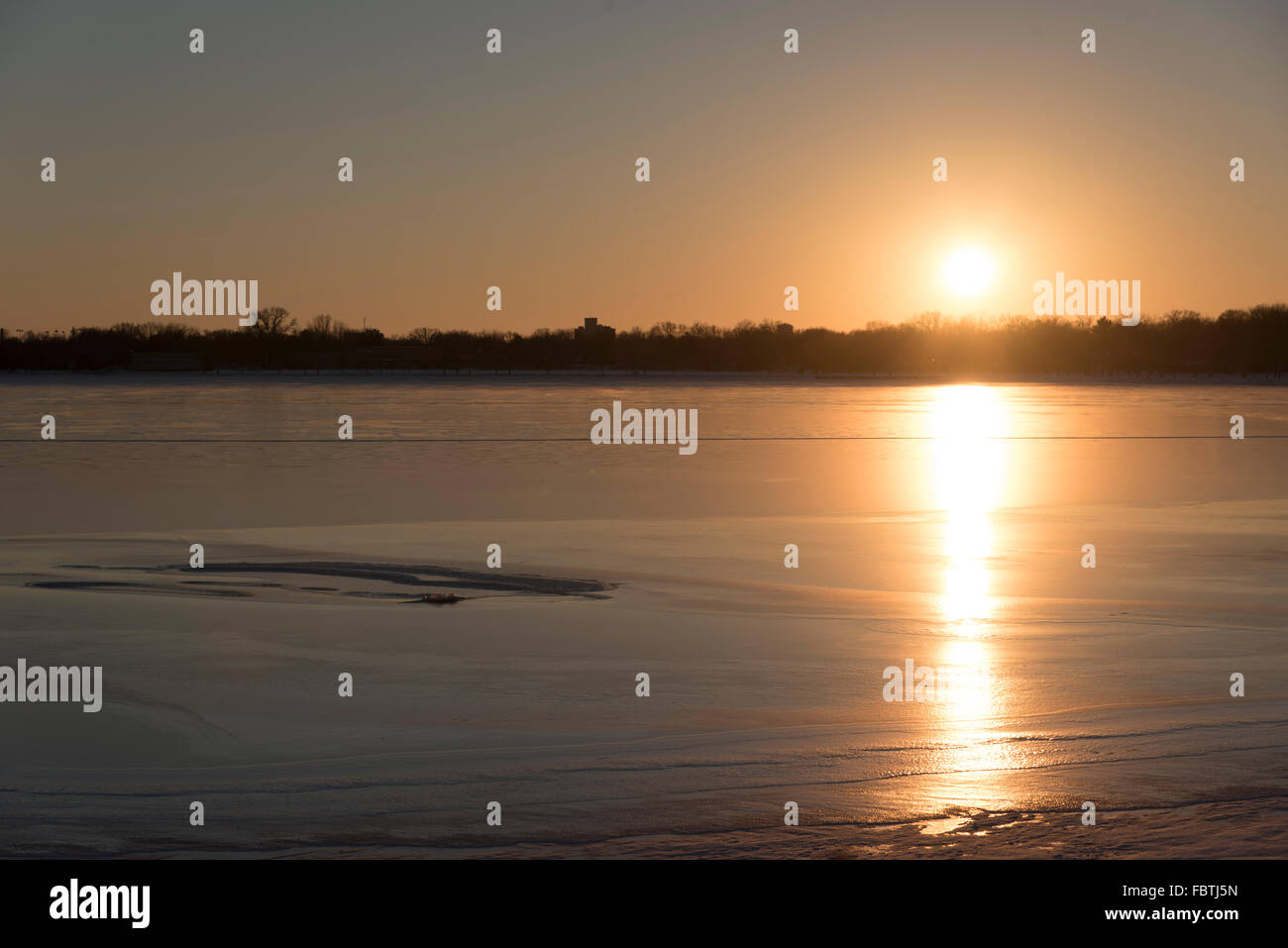 The sun sets over of frozen lake, without snow cover, so the sun ...