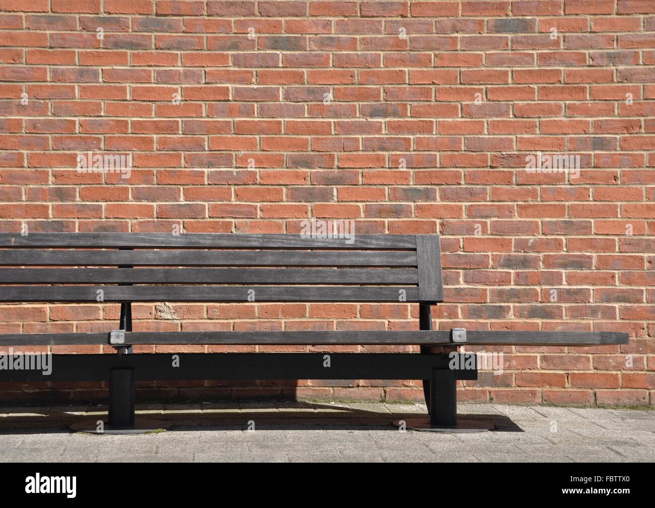 wooden bench against a brick wall building Stock Photo - Alamy