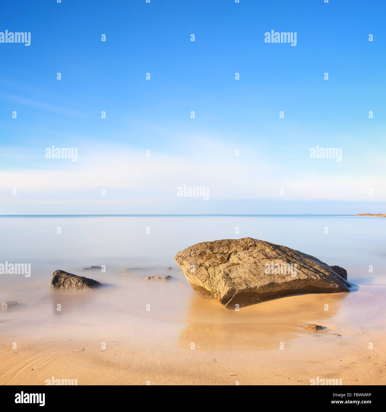 A flat rock on a golden sand beach and blue ocean. Long exposure ...