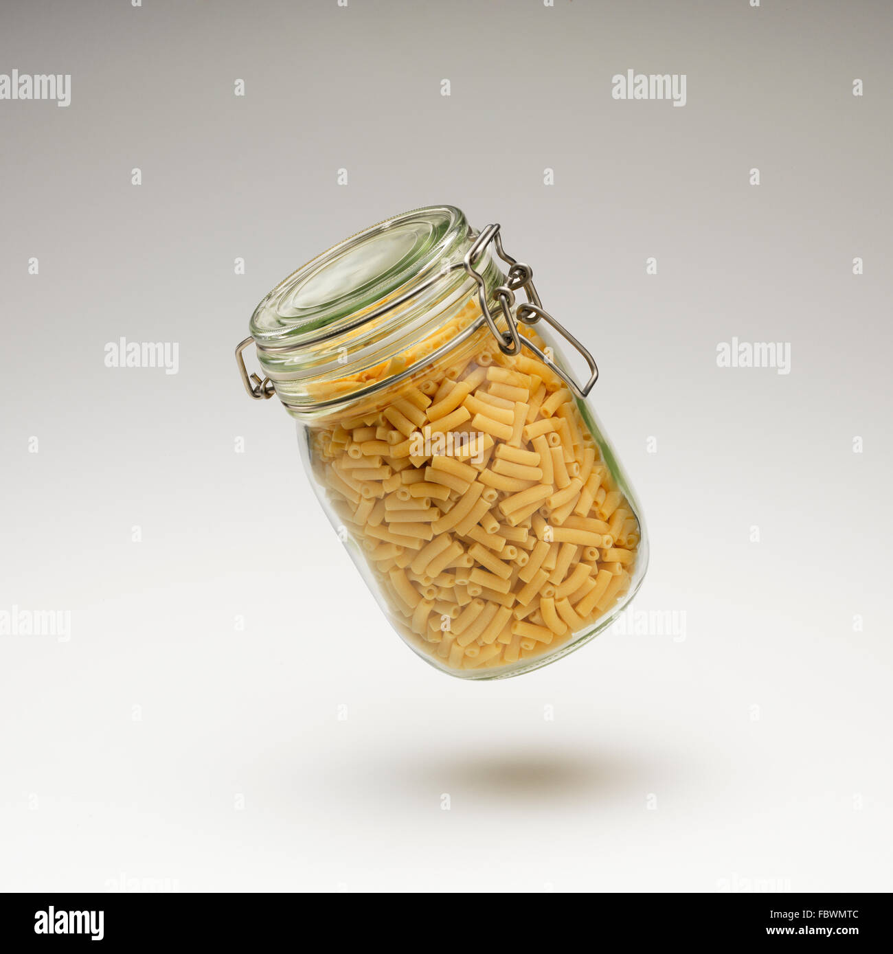a glass jar of dried pasta falling or floating on a white background ...