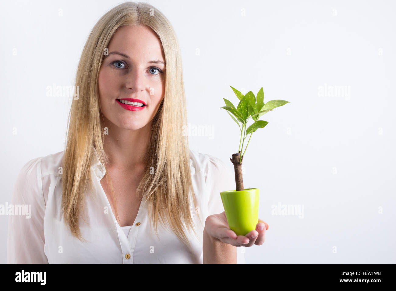 Blond woman holding a small green tree Stock Photo - Alamy