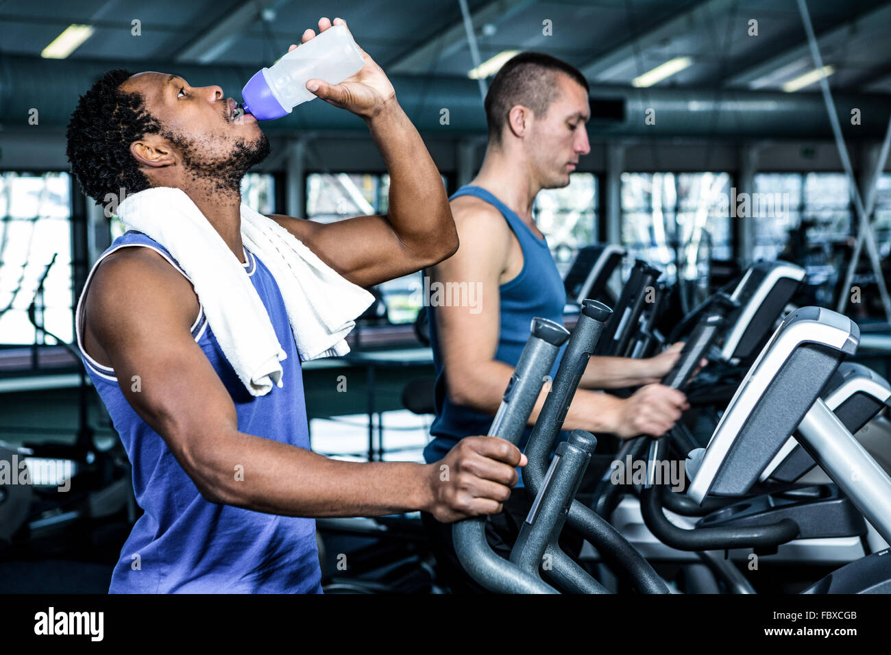 Man drinking water while using elliptical machine Stock Photo - Alamy