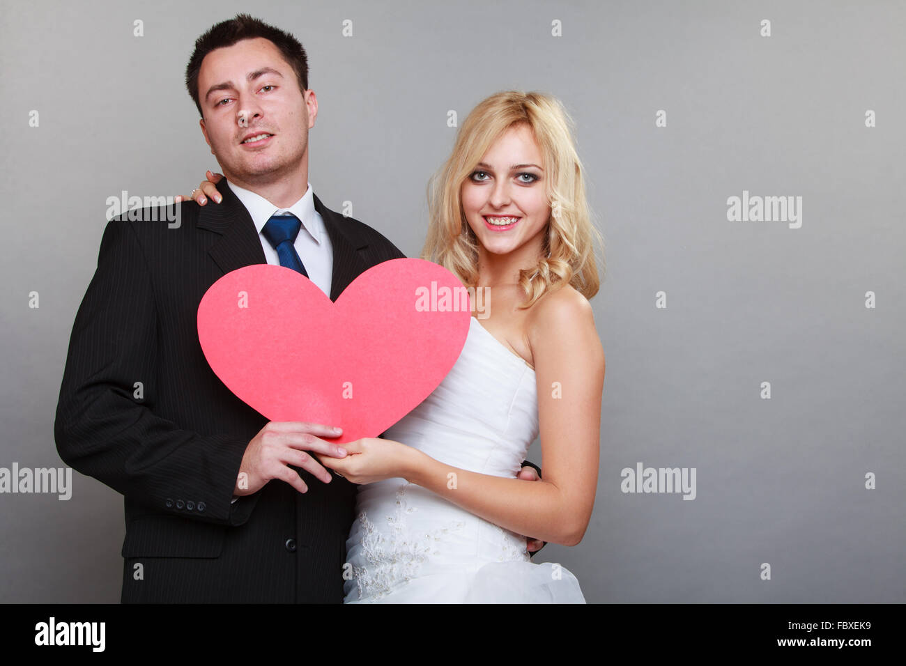 Portrait of happy bride and groom with red heart on gray Stock Photo ...