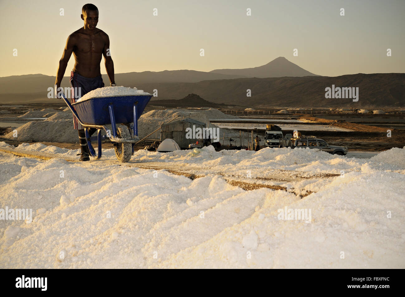 Young African man pushes a wheelbarrow full of salt in a saline on the ...