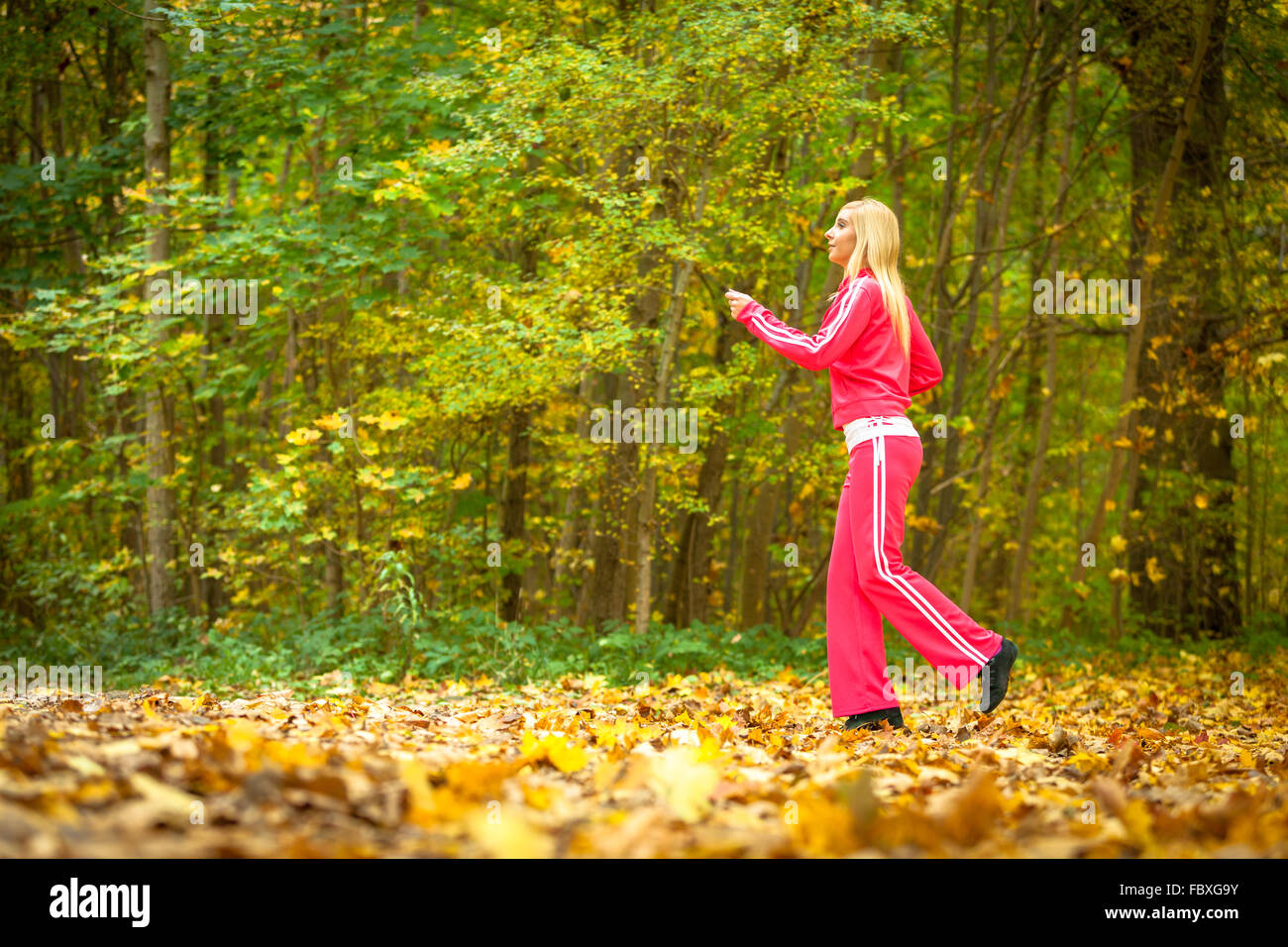 Blonde girl young woman running jogging in autumn fall forest park ...