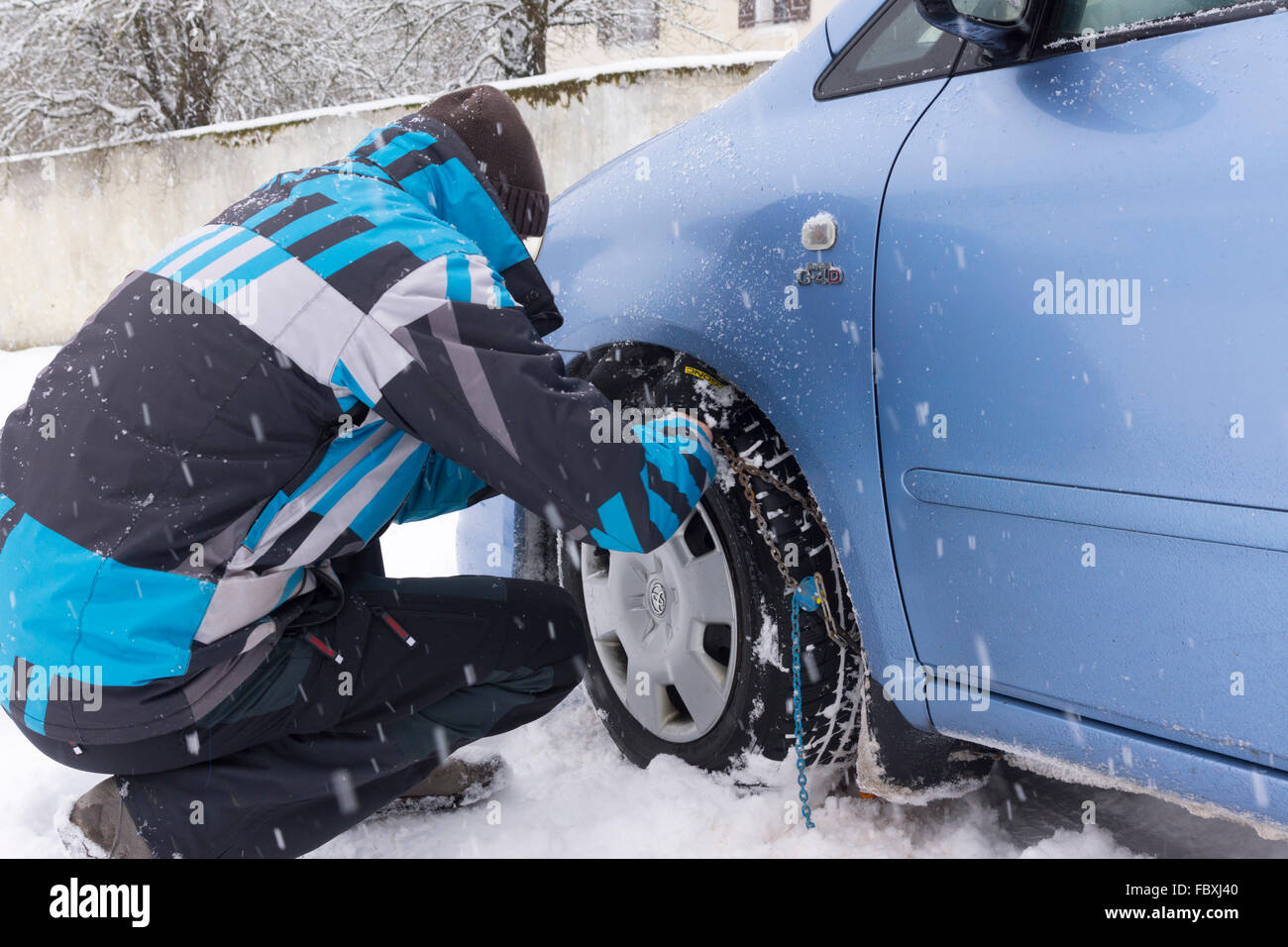A man fitting / attaching snow chains to a car tyre for better traction ...