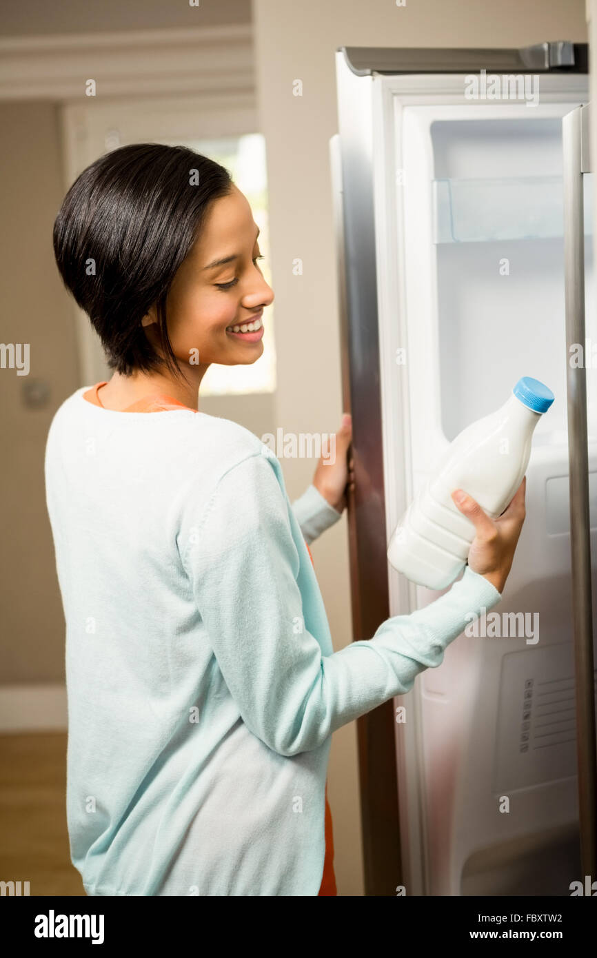 Smiling brunette holding milk bottle with open refrigerator Stock Photo ...