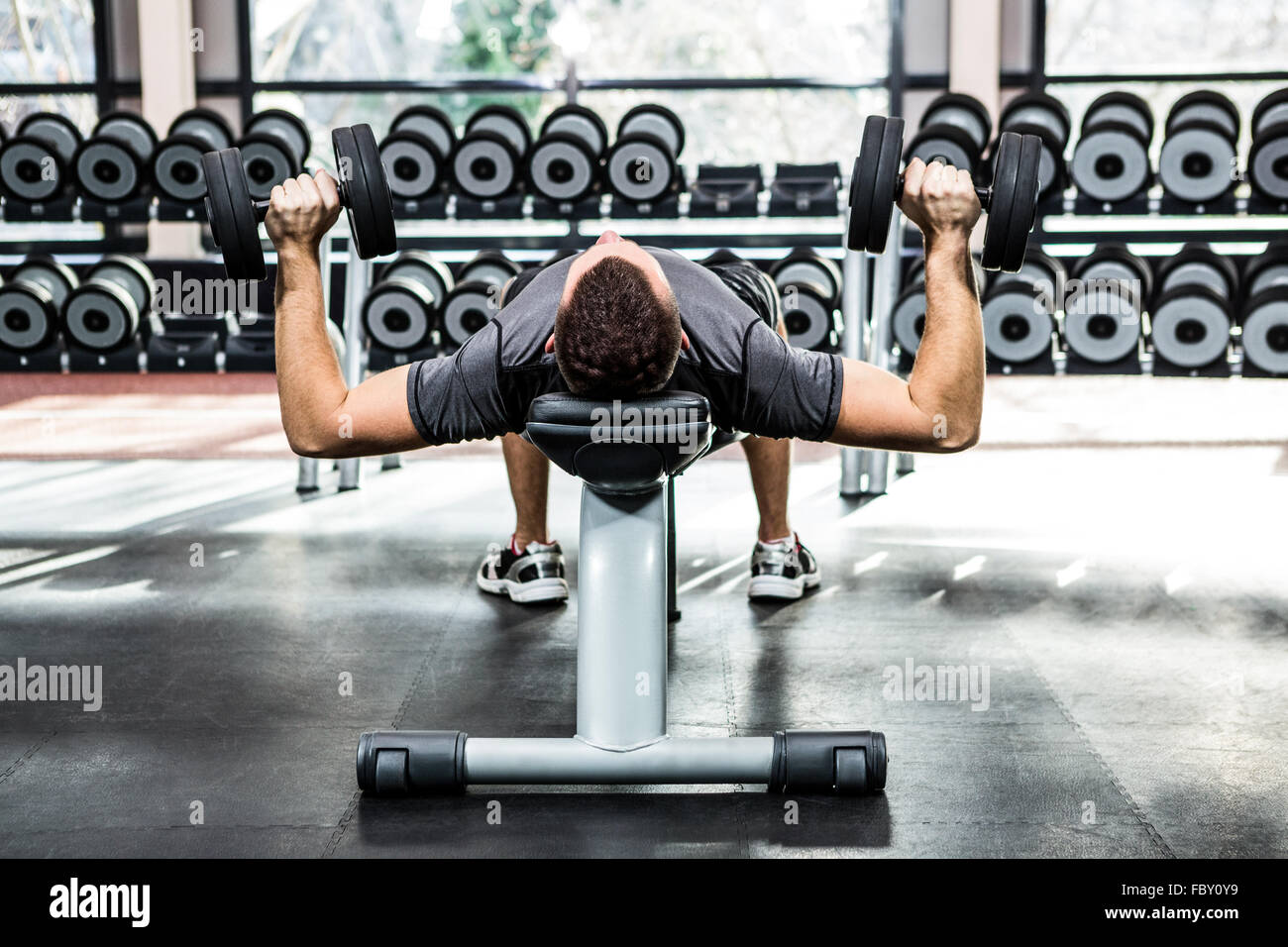 Muscular man lifting dumbbells while lying on bench Stock Photo - Alamy