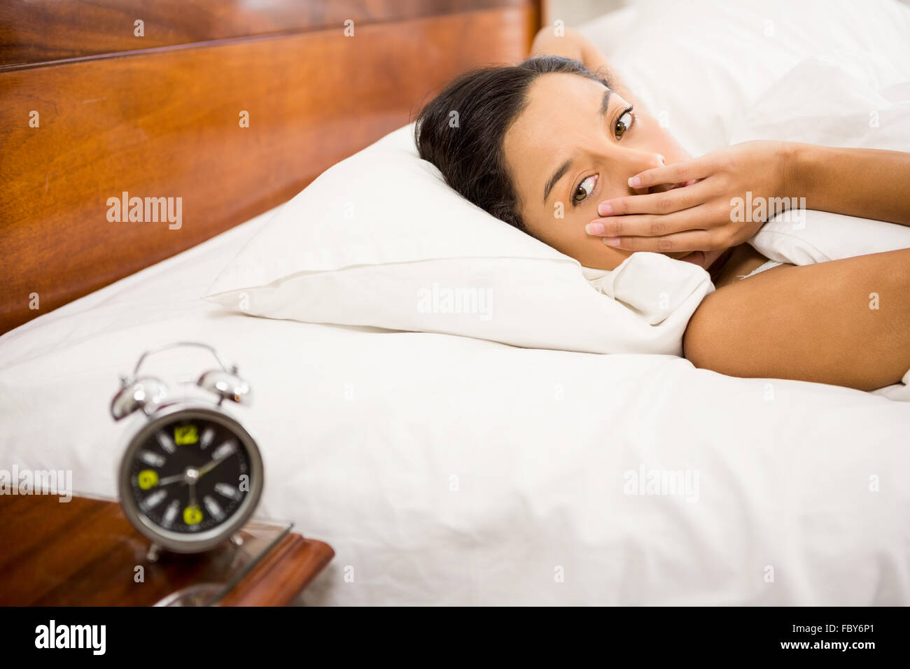 Brunette in the bed looking at alarm clock on the table Stock Photo - Alamy