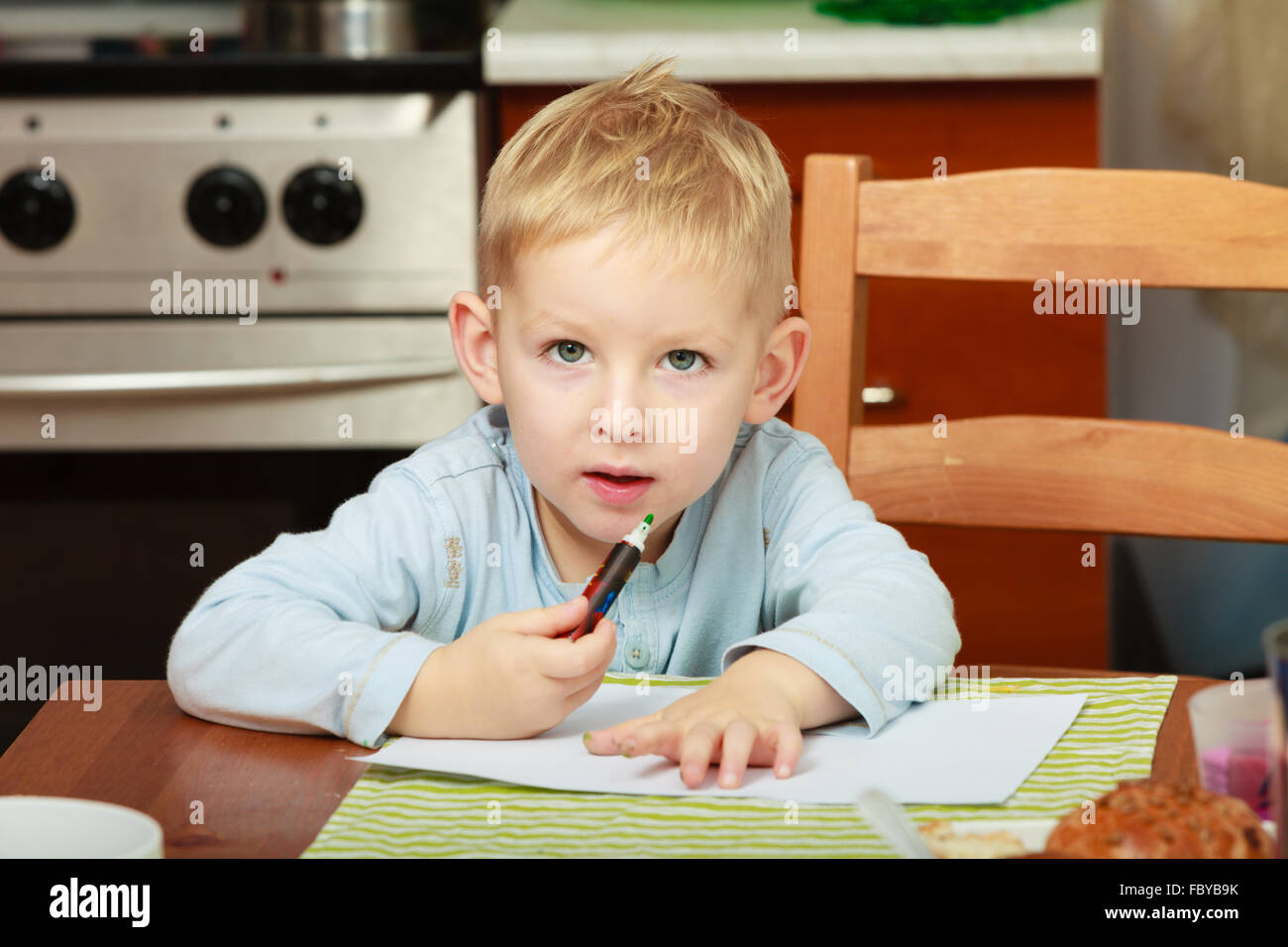 Blond boy child kid drawing with marker on piece of paper. At home ...