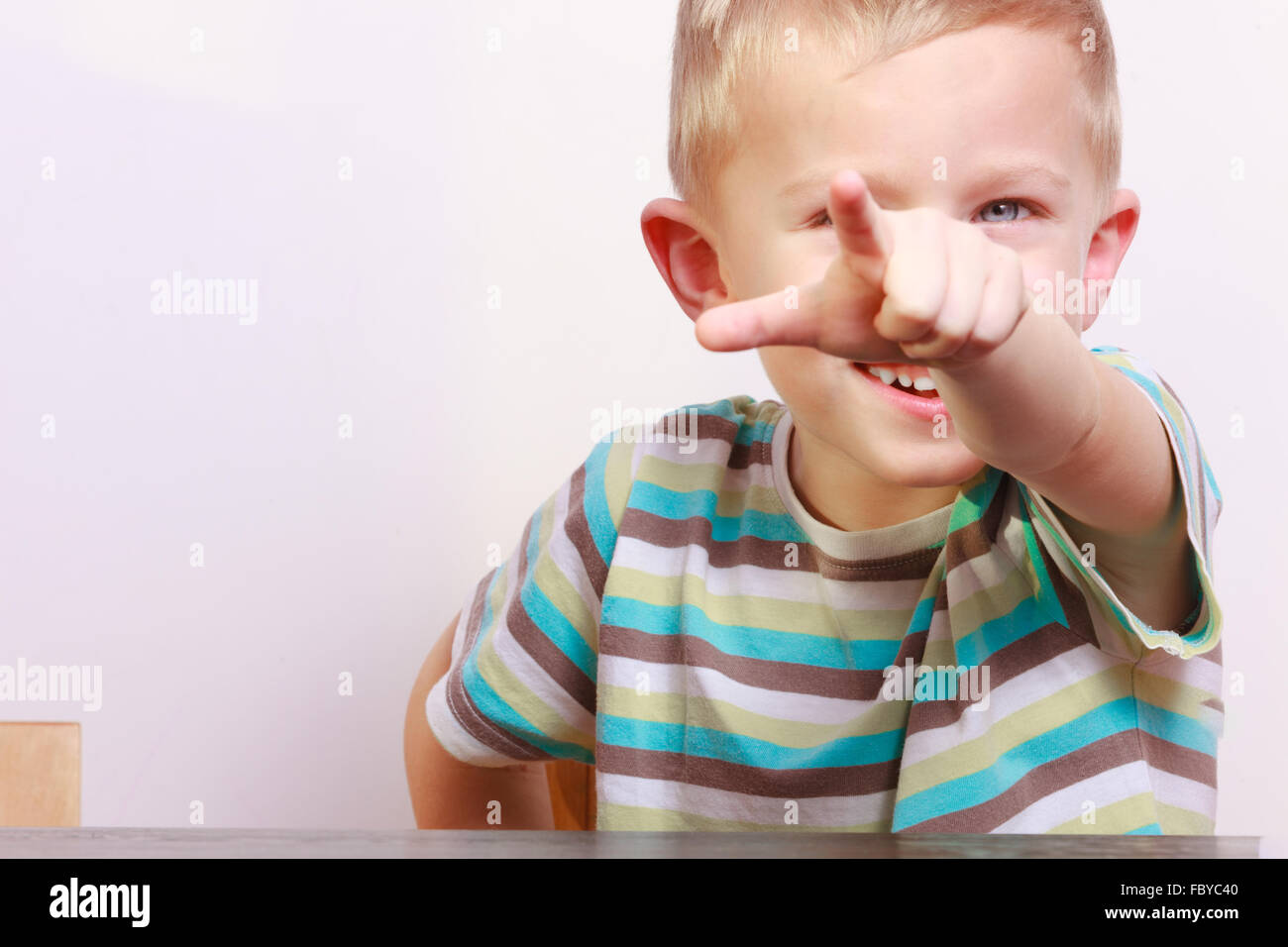 Portrait of happy blond boy child kid pointing at you at the table ...