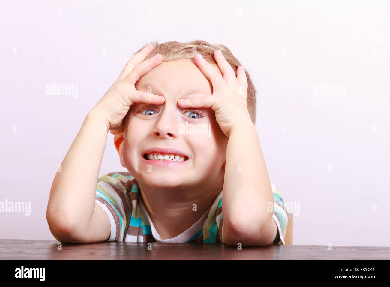 Portrait of surprised angry emotional blond boy child kid at the table ...