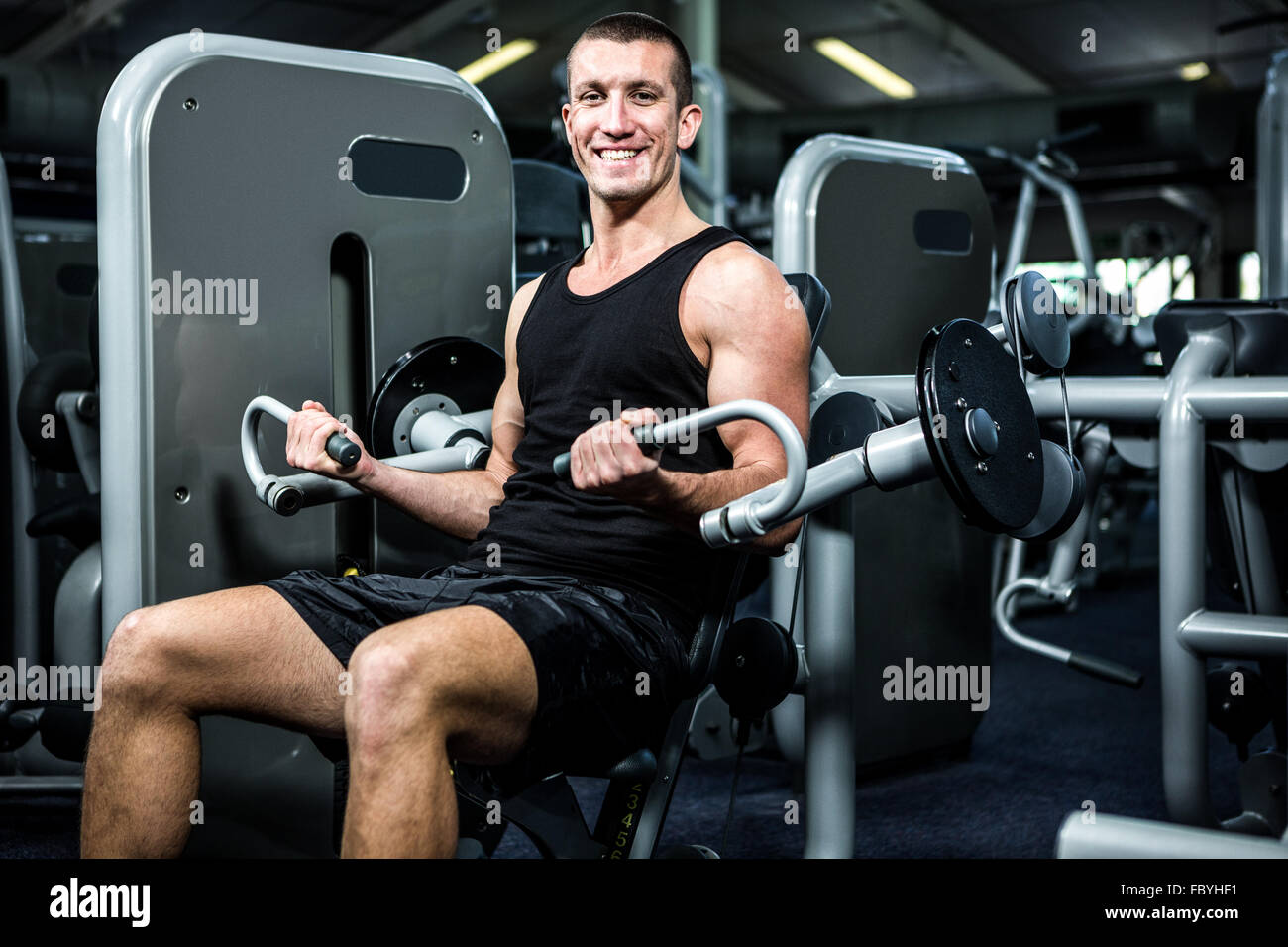 Smiling muscular man using exercise machine Stock Photo - Alamy