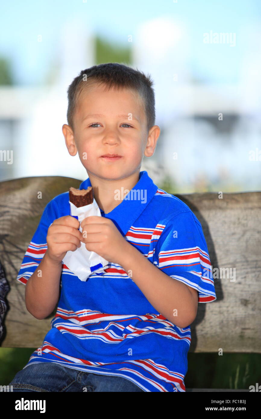 boy sitting on bench in park eating chocolate Stock Photo - Alamy